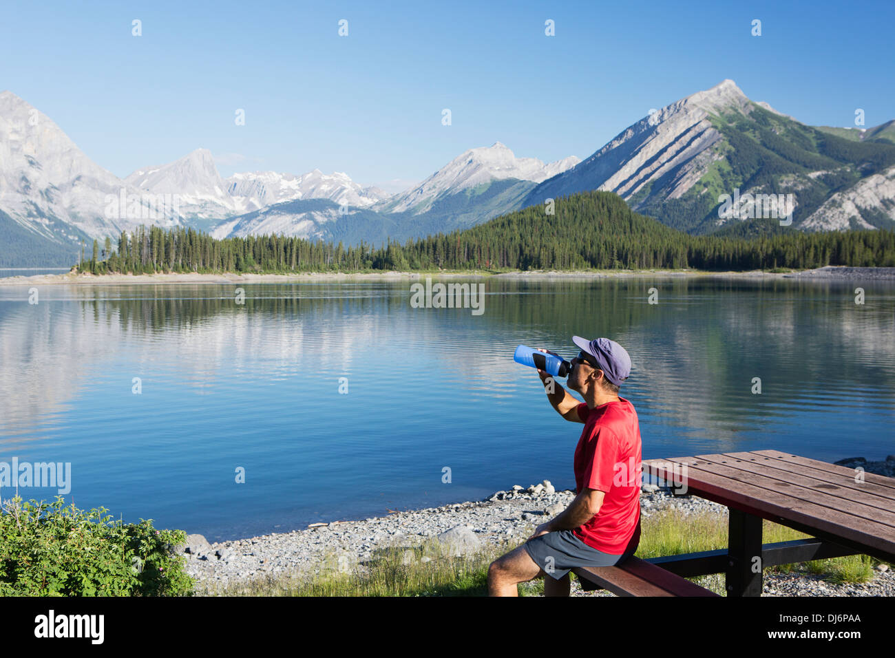 A Man Drinks From A Water Bottle On The Edge Of A Lake Overlooking The ...