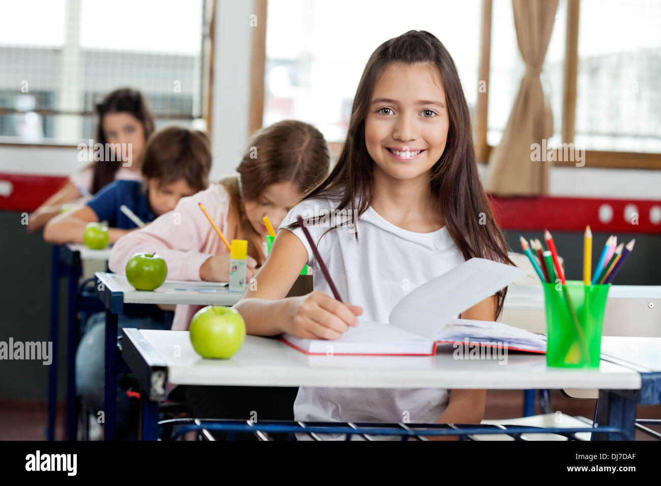 Schoolgirl Writing In Book At Classroom Stock Photo - Alamy