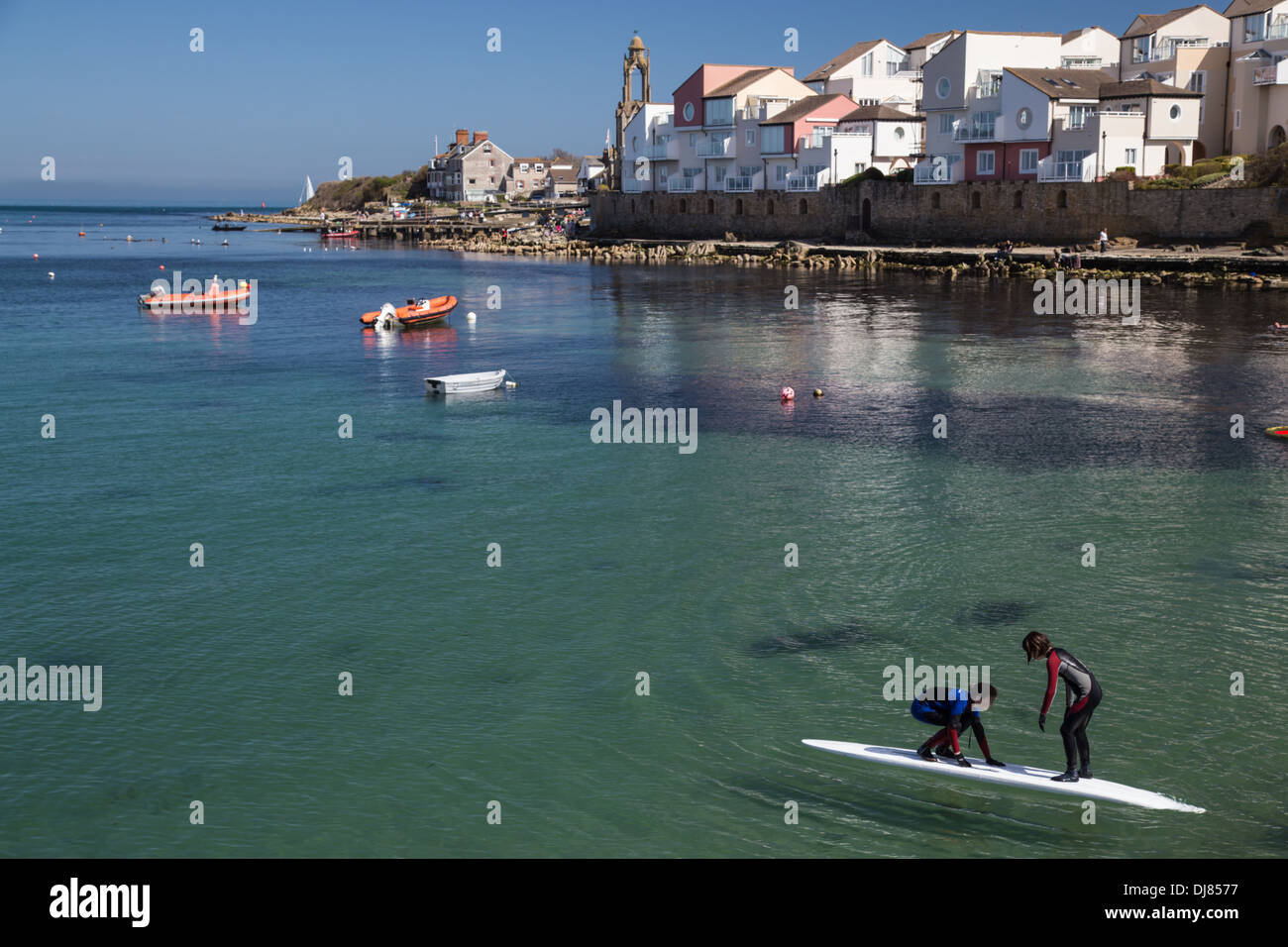 Two girls standing on surf board at Swanage Beach, Dorset, England ...