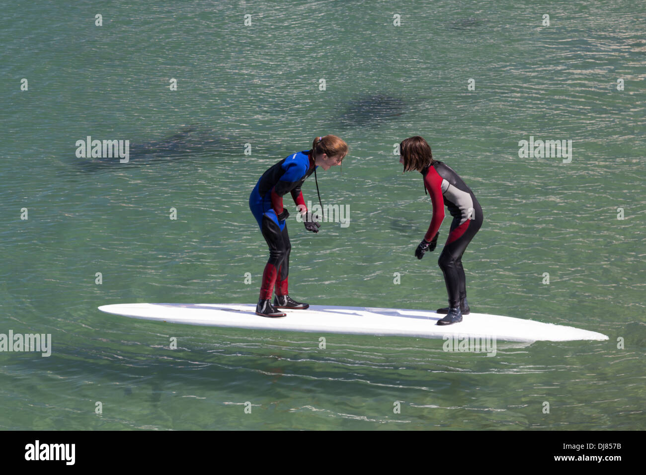 Two girls standing on surf board at Swanage Beach, Dorset, England ...