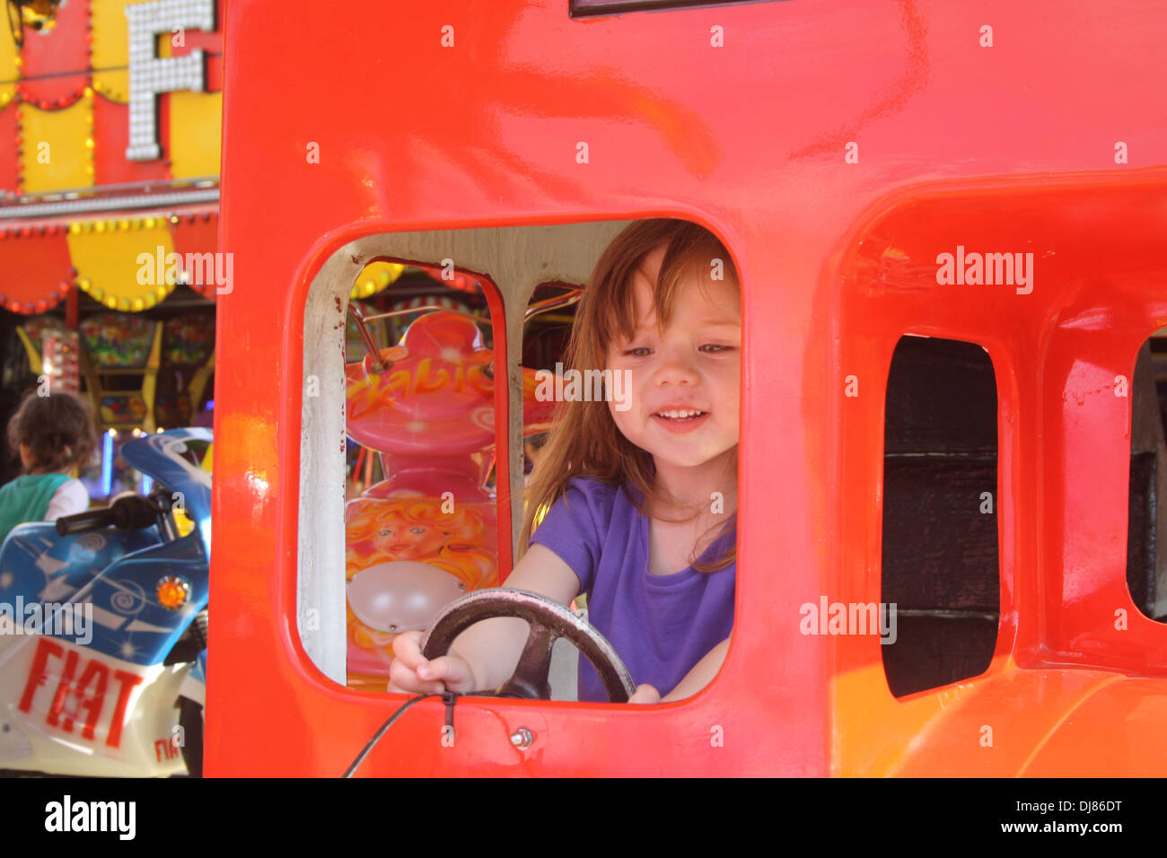 Girl driving a red bus at a fairground Stock Photo - Alamy