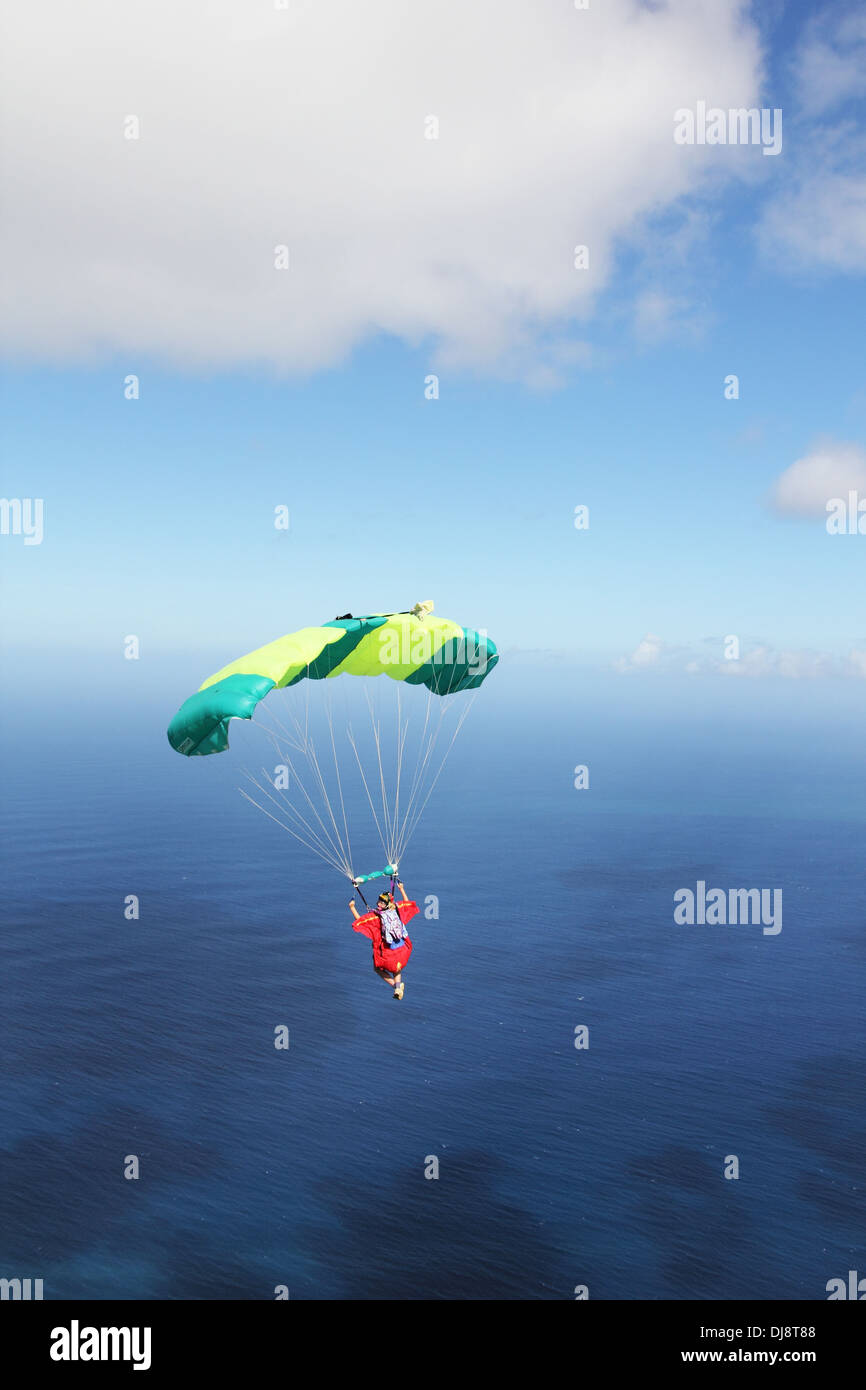 Skydiver under canopy is flying over the deep sea under clouds. Thereby ...