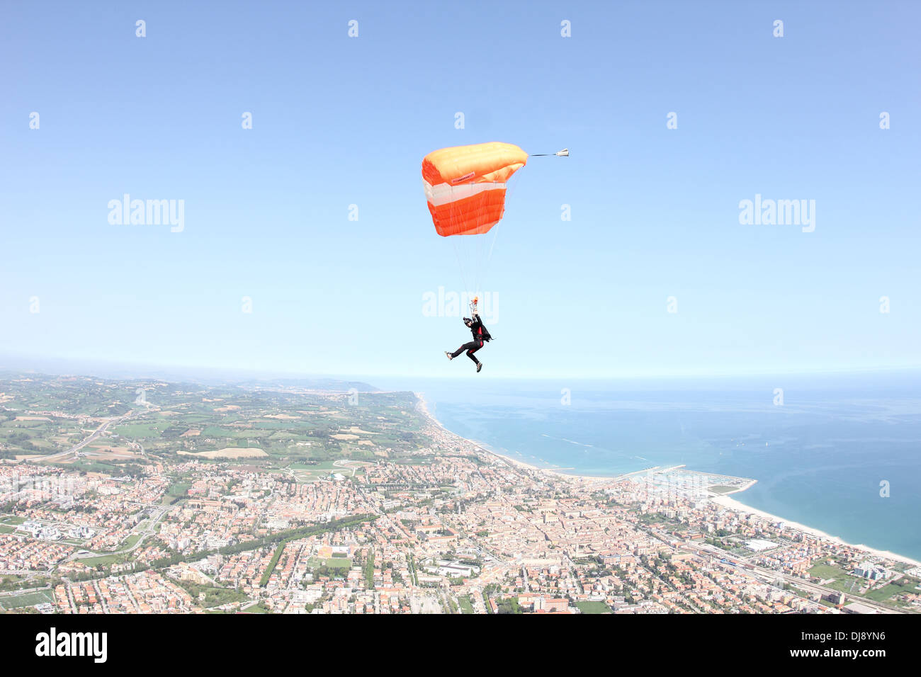 Skydiver under canopy is flying high over a big city next to the sea ...