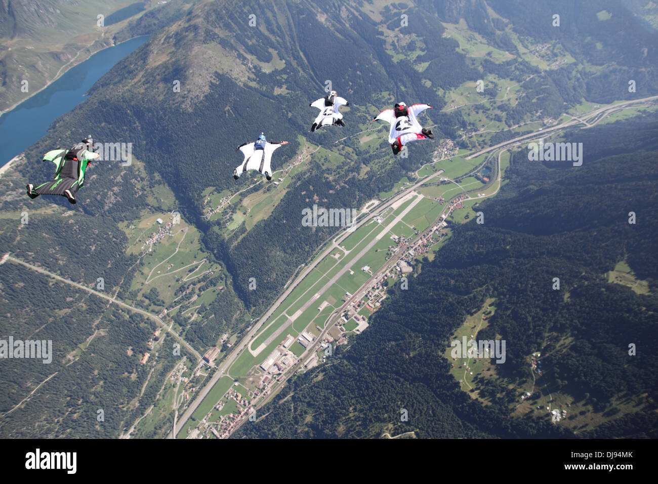 Wingsuit skydivers are flying together in an arrow formation over a ...