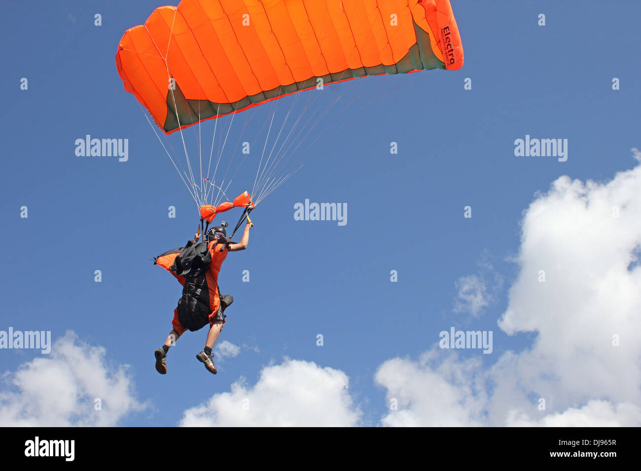 Skydiver under canopy is flying high in the blue sky between clouds ...