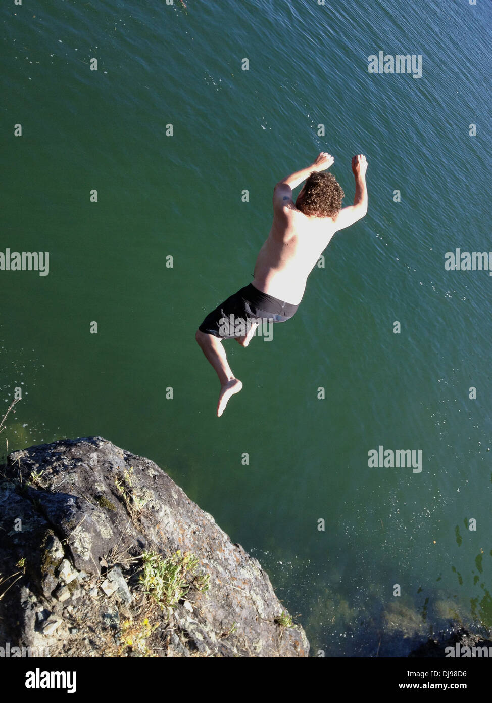 Caucasian man jumping off rock into lake Stock Photo - Alamy
