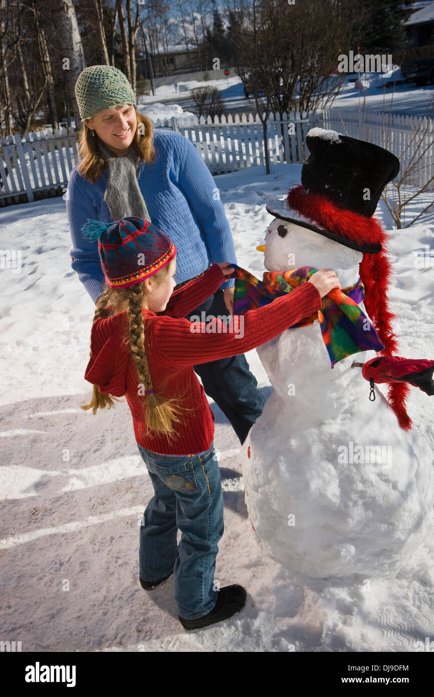 Mother Helping Daughter Decorate A Snowman In The Front Yard Of An ...