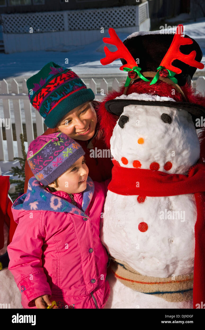 Hispanic Mother Helping Daughter Decorate A Snowman In The Front Yard ...