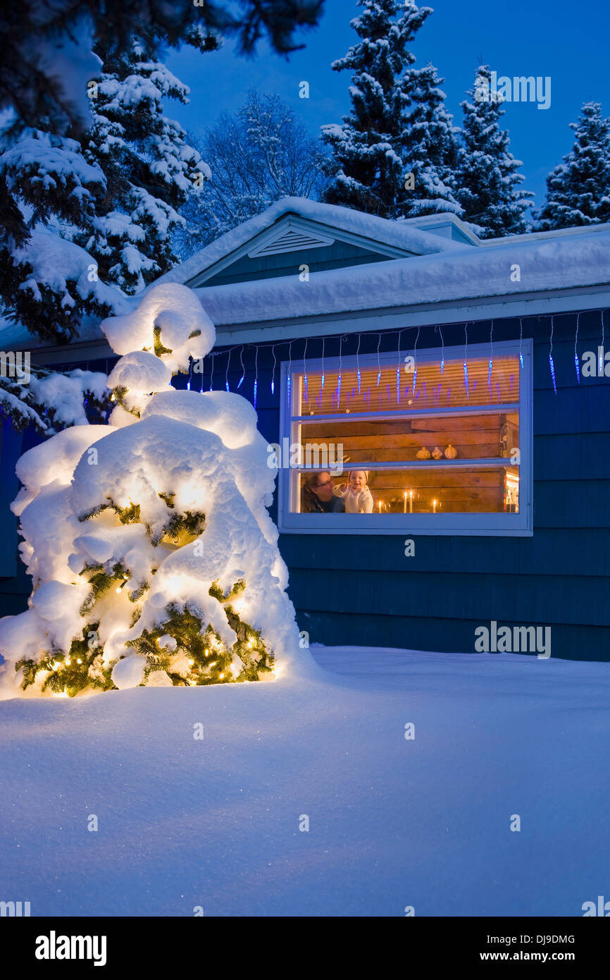Family Looks Out Through Window At A Decorated & Snowcovered Christmas ...