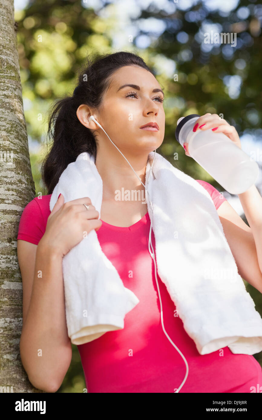 Gorgeous brunette woman leaning against a tree and drinking water while ...