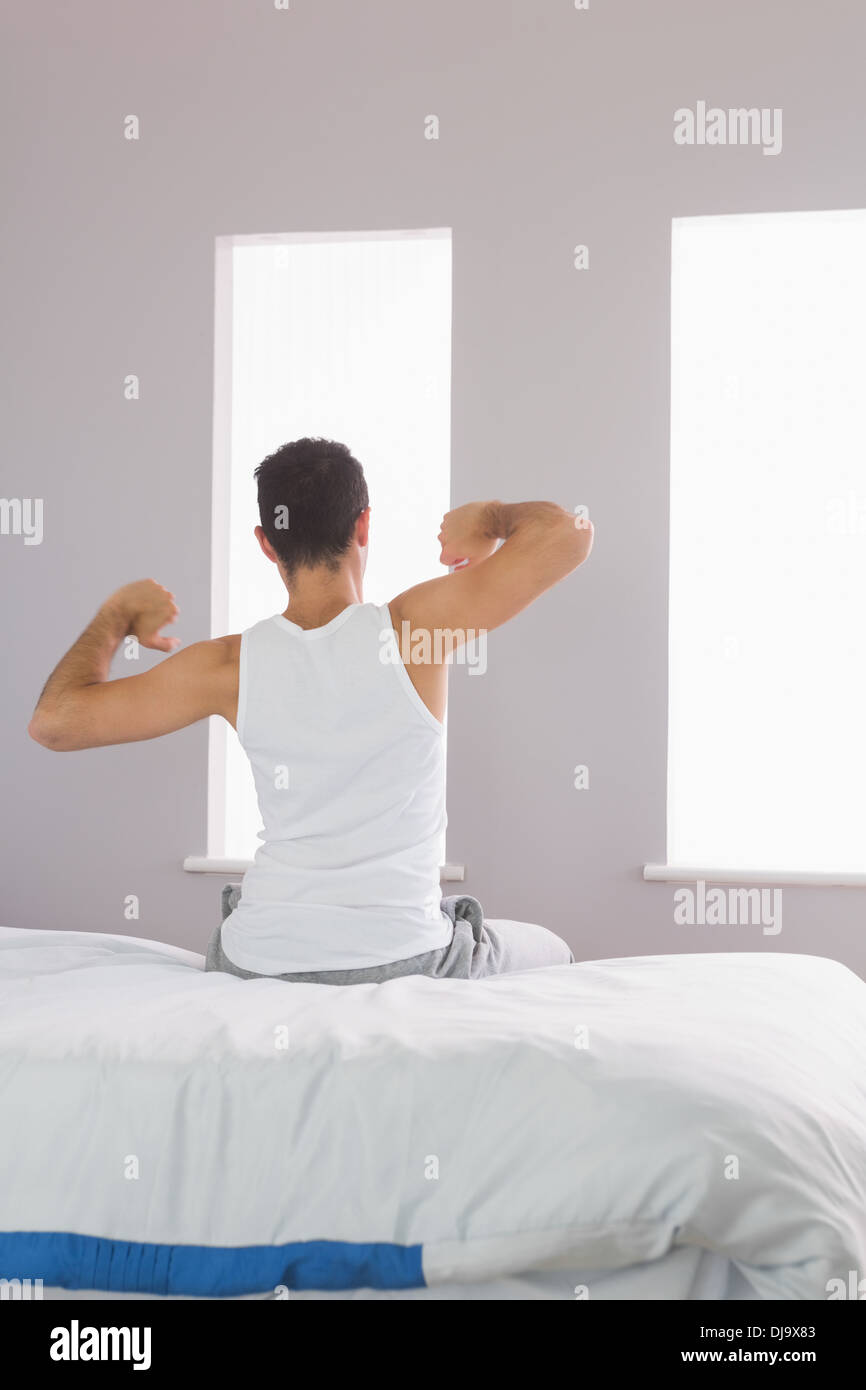 Rear view of man in pyjamas sitting on bed stretching his arms Stock ...