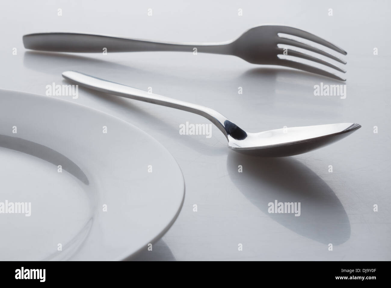 a fork and a spoon next to a white on a scratchy table surface. Focus ...