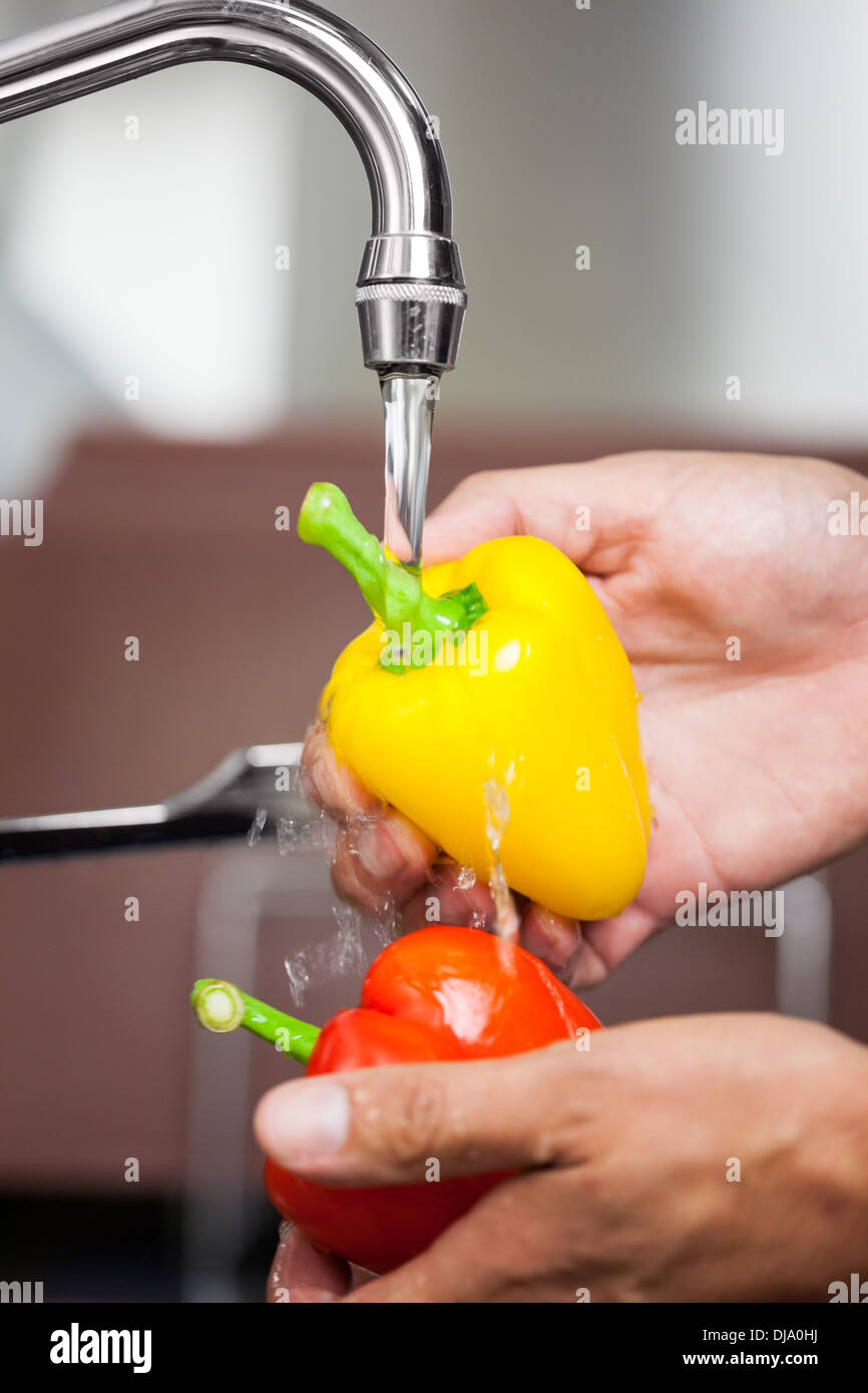 Kitchen porter washing red and yellow pepper under running tap Stock ...