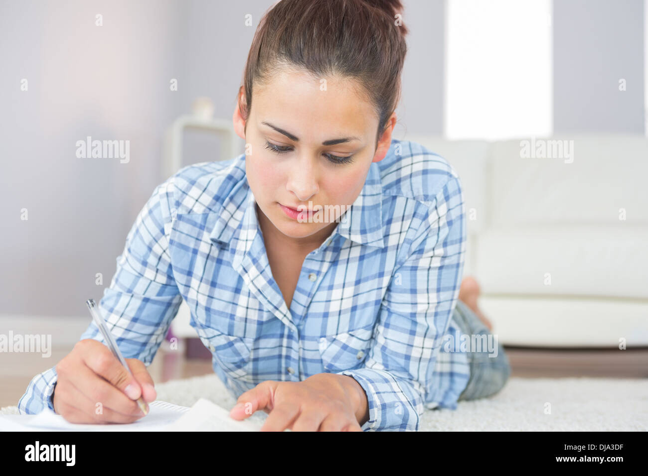 Brunette young student doing assignments lying on a carpet in the ...