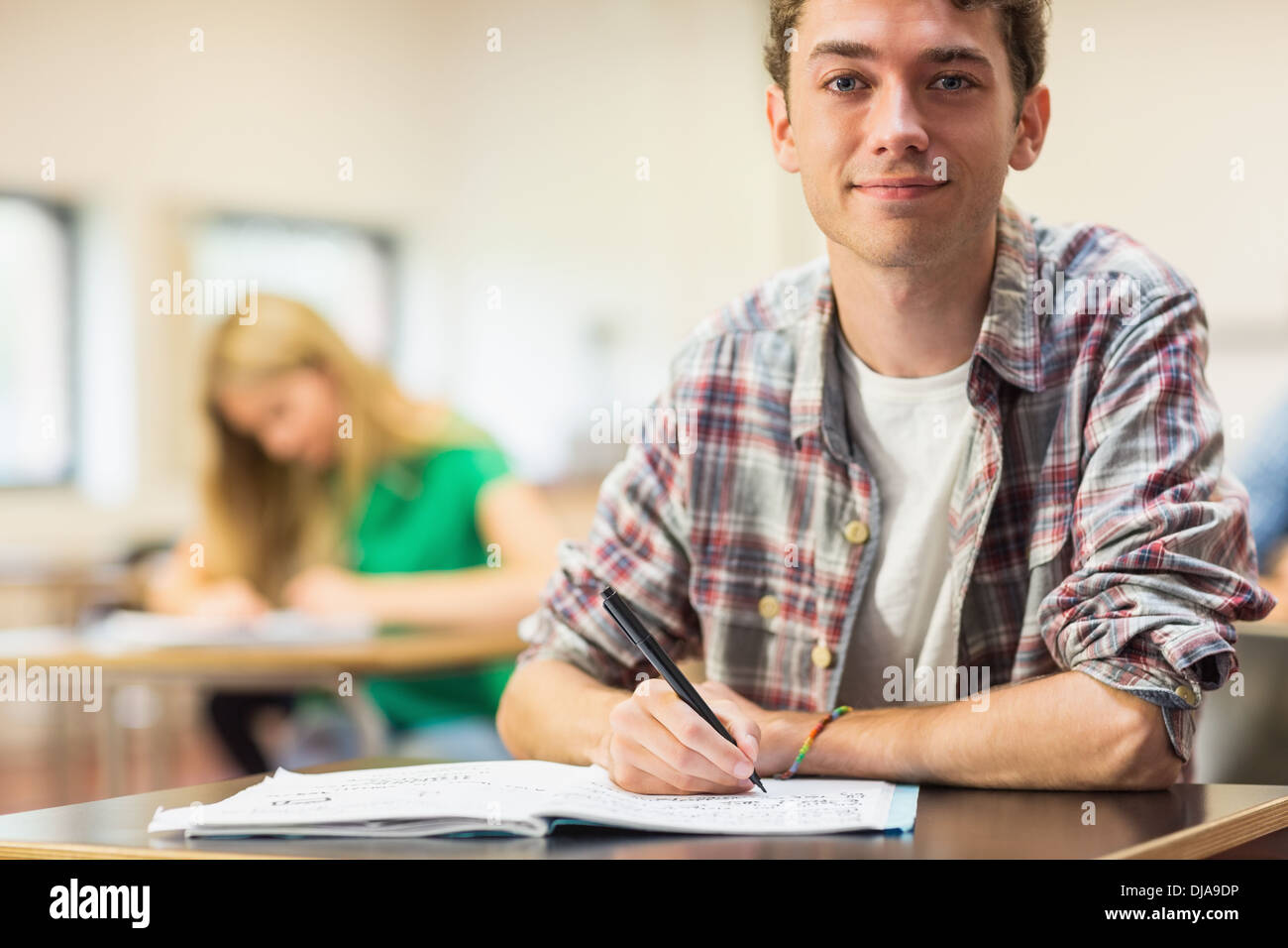Smiling student with others writing notes in classroom Stock Photo - Alamy