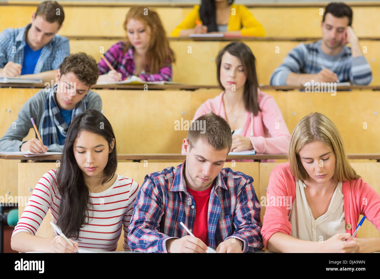 Students sitting at the lecture hall while writing Stock Photo - Alamy