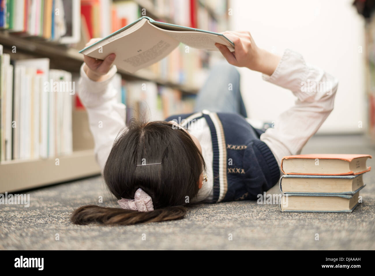 Young girl student laying on the library floor and reading a stack of ...