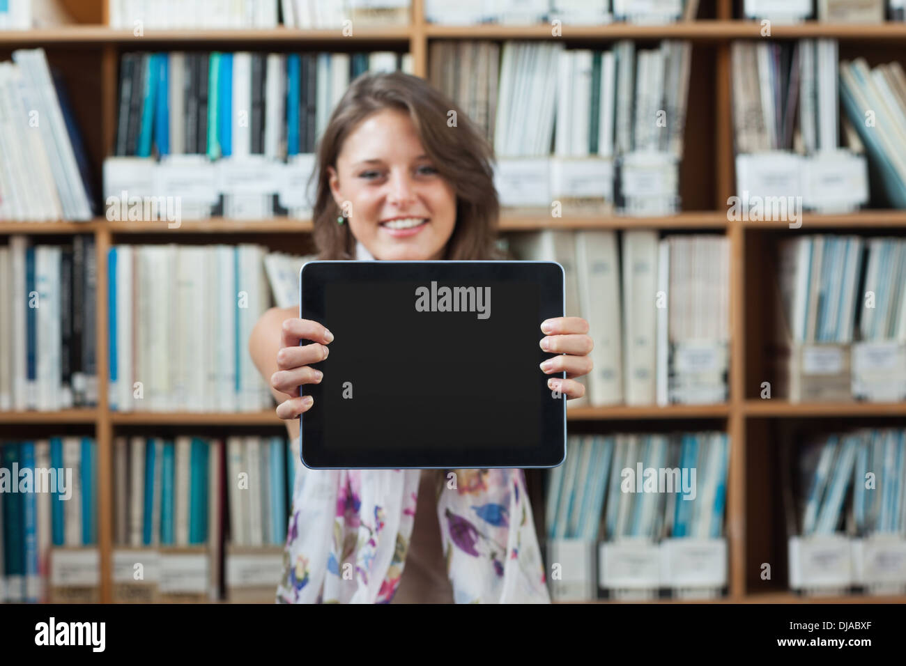 Female student against bookshelf holding out tablet PC in library Stock ...