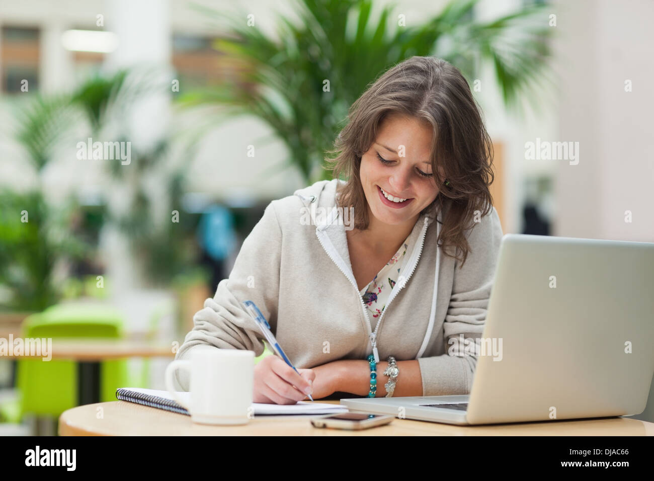 Student doing homework by laptop at cafeteria table Stock Photo - Alamy
