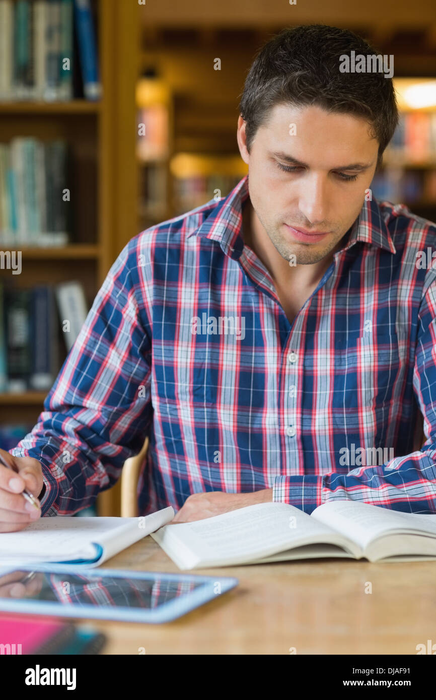 Male student writing notes at desk in the library Stock Photo - Alamy