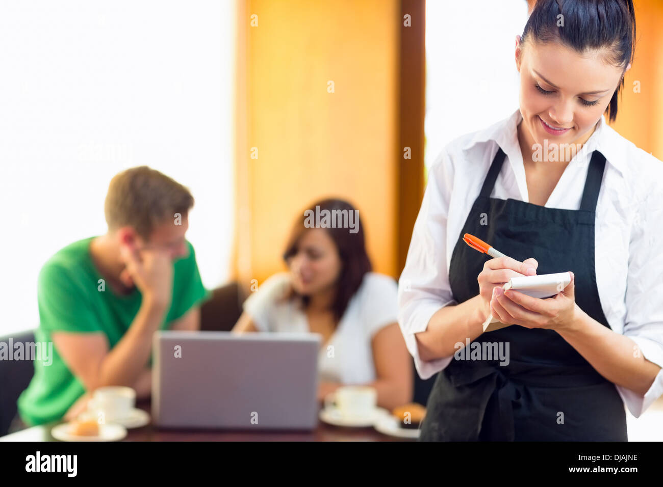 Waitress writing an order with students using laptop at coffee shop ...