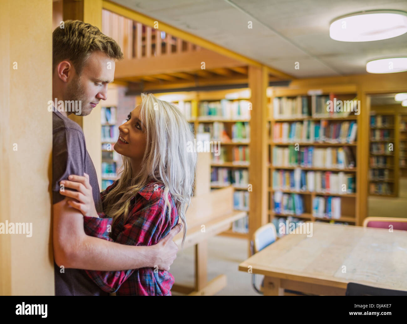 Young romantic couple with bookshelf at distance in library Stock Photo ...