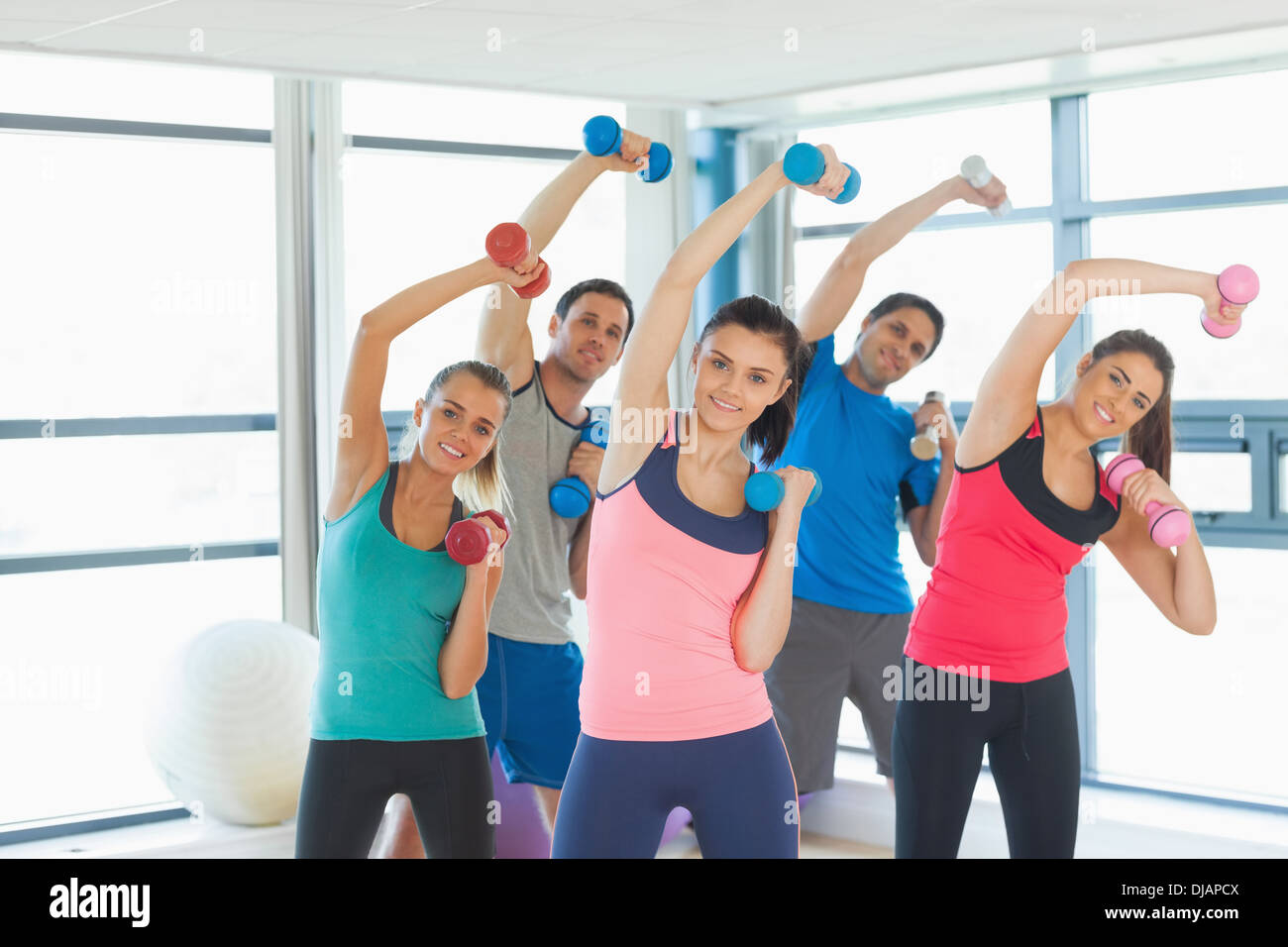 People lifting dumbbell weights with trainer in gym Stock Photo - Alamy
