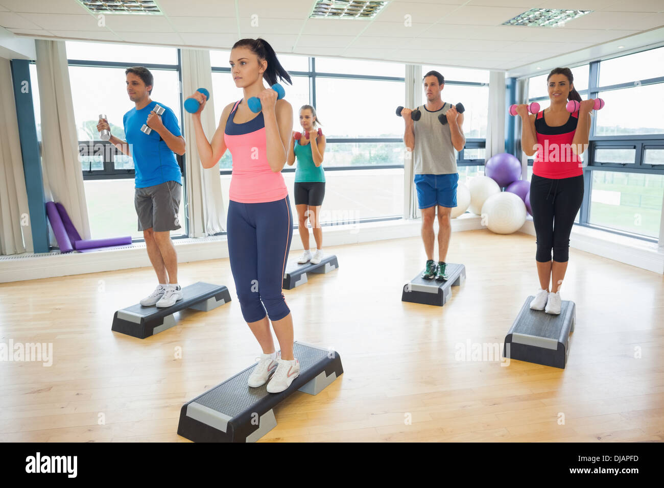 Instructor with fitness class performing step aerobics exercise with ...