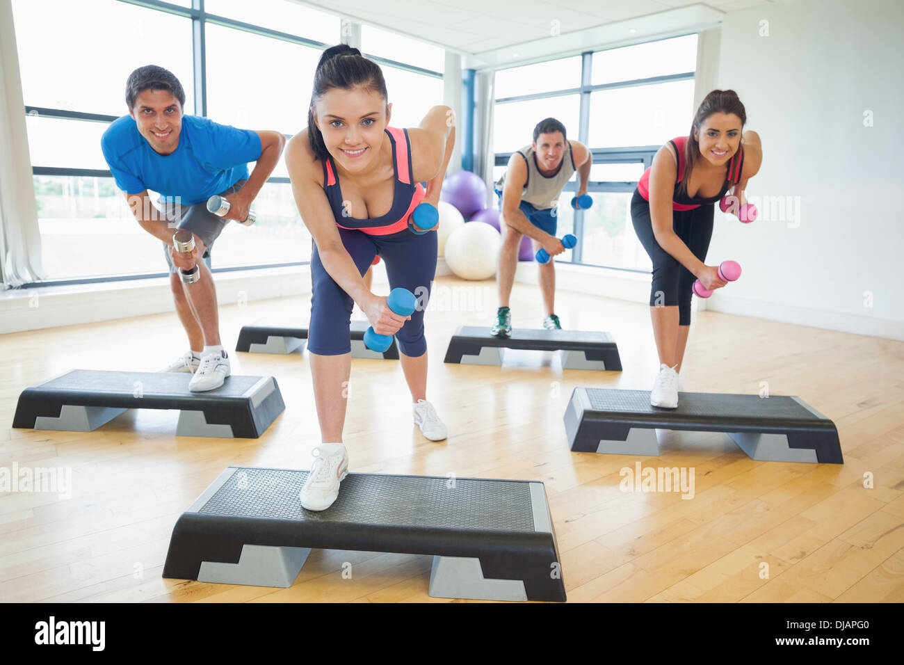 Instructor with fitness class performing step aerobics exercise with ...
