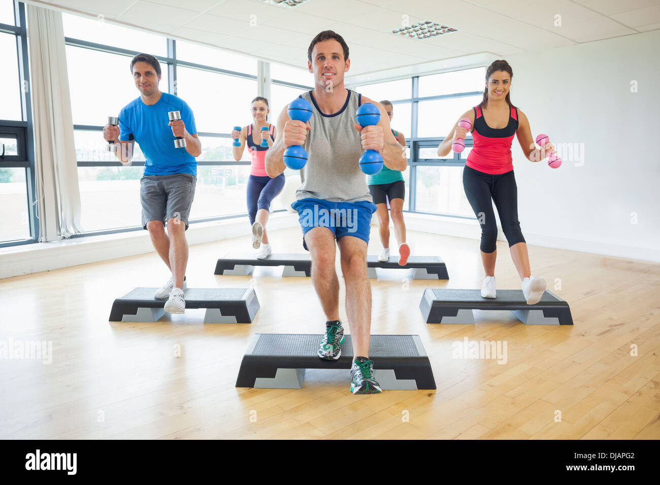 Instructor with fitness class performing step aerobics exercise with ...