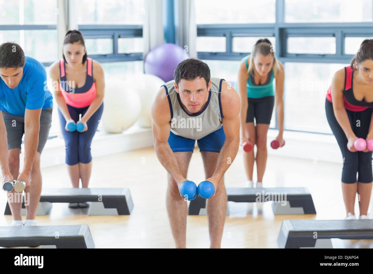 Instructor with fitness class performing step aerobics exercise with ...