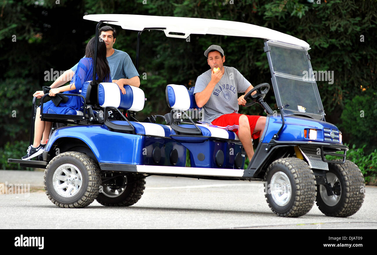 Adam Sandler eating an apple as he drives a golf cart in Brentwood with ...