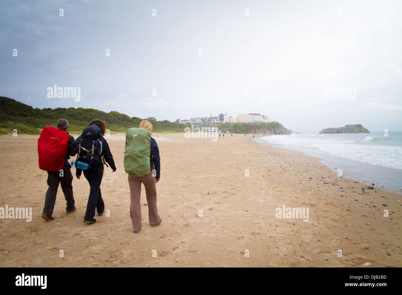 Three adults walking towards Tenby on coastal path Pembrokeshire Wales ...