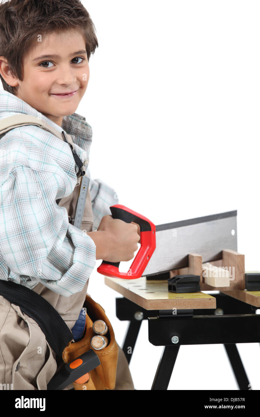 Young boy dressed as an adult carpenter cutting wood with a saw Stock ...