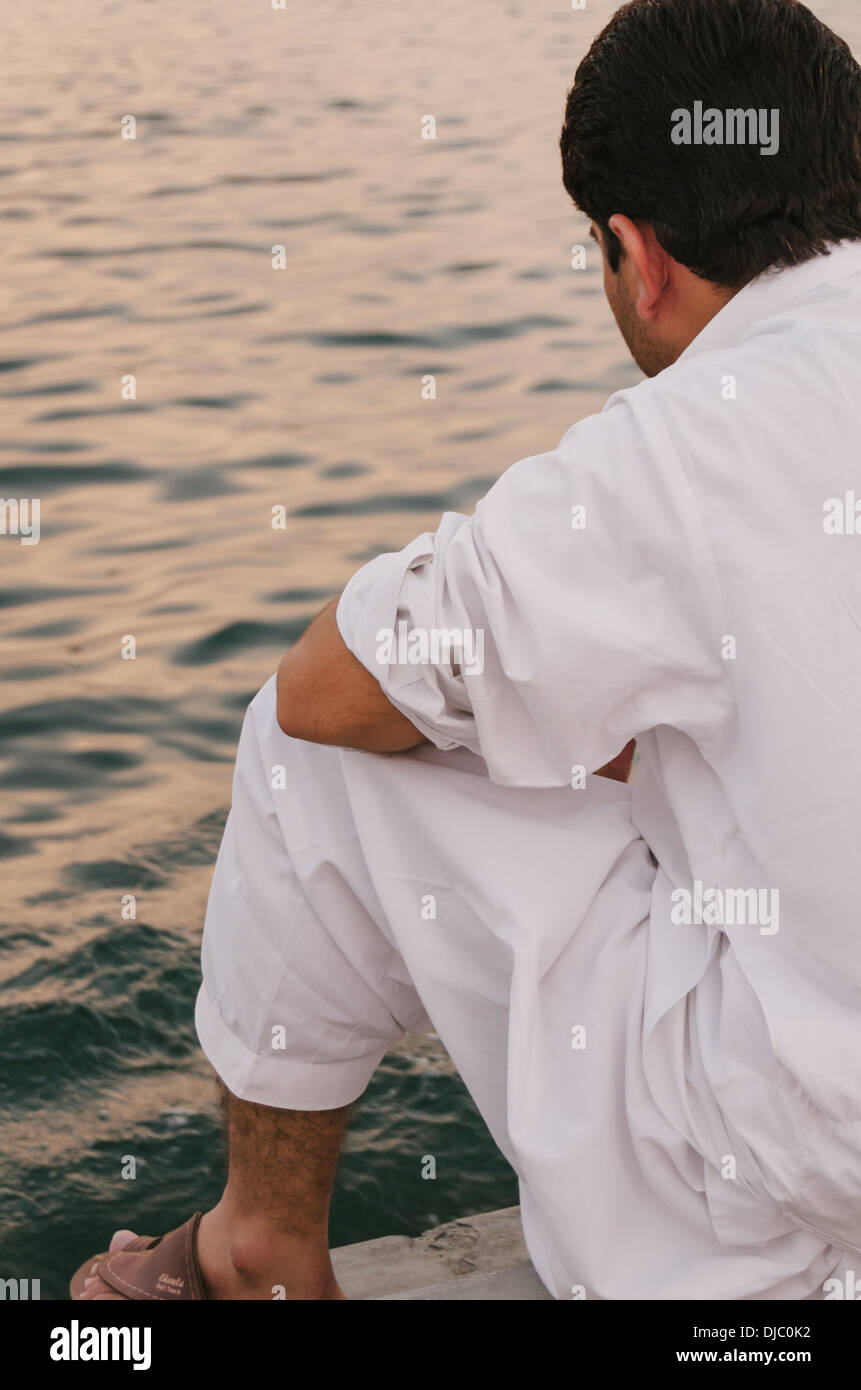 Arab man in traditional clothing meditating by the undulating waters of ...