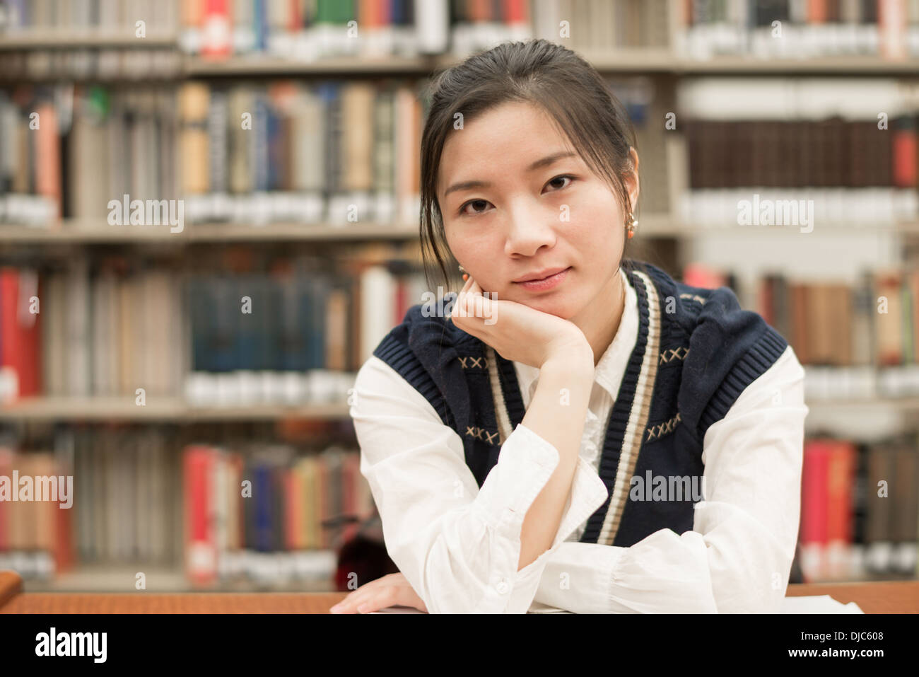 Pretty female student sitting at a desk with a open book studying in ...