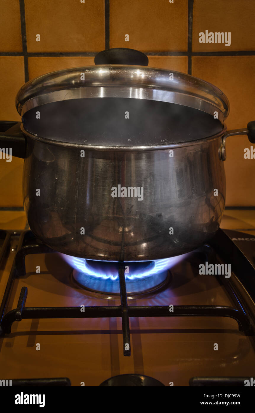 Stainless steel saucepan on gas hob high heat boiling over with steam ...
