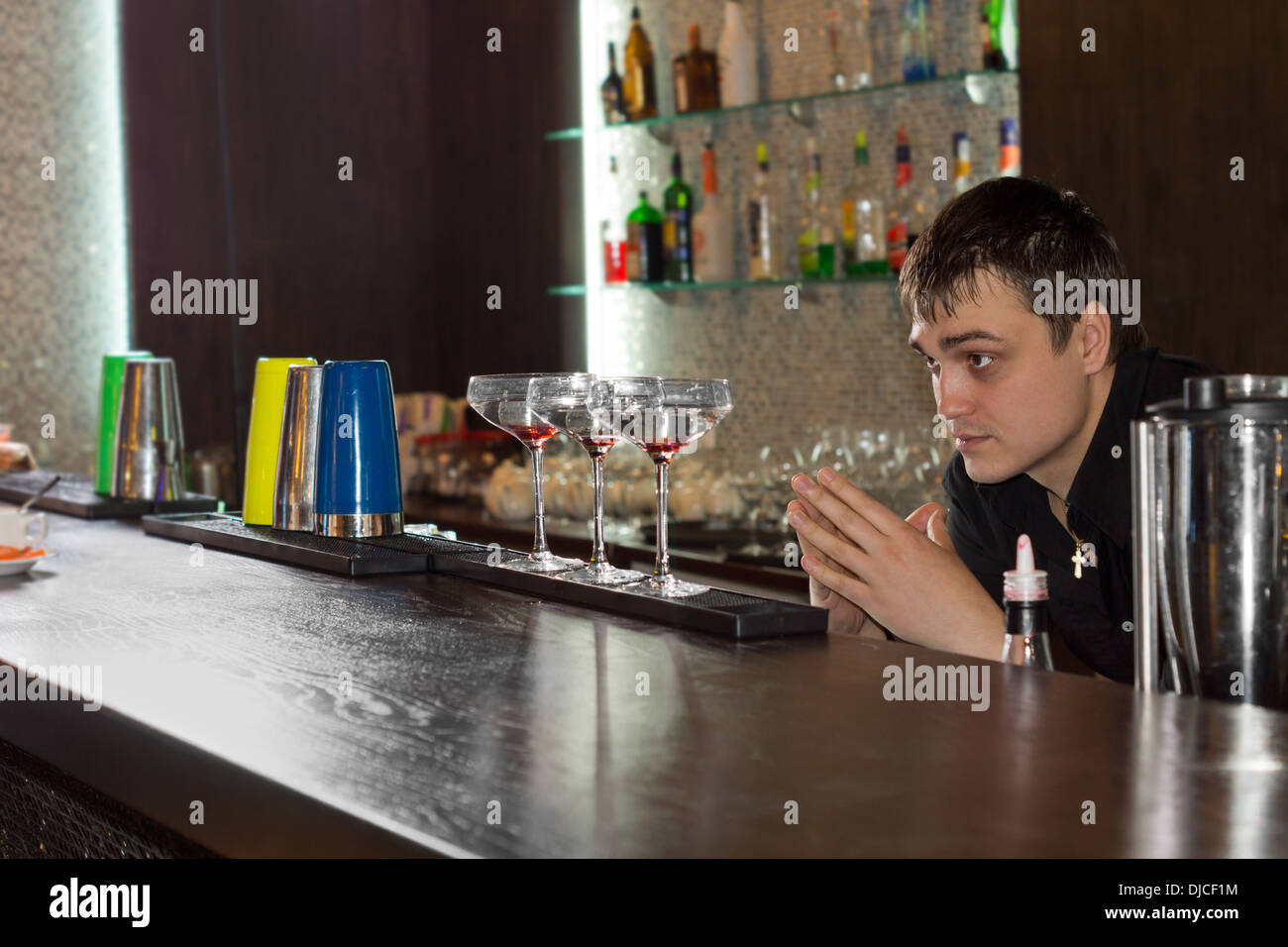 Professional young barman checking three saucer glasses filled with ...