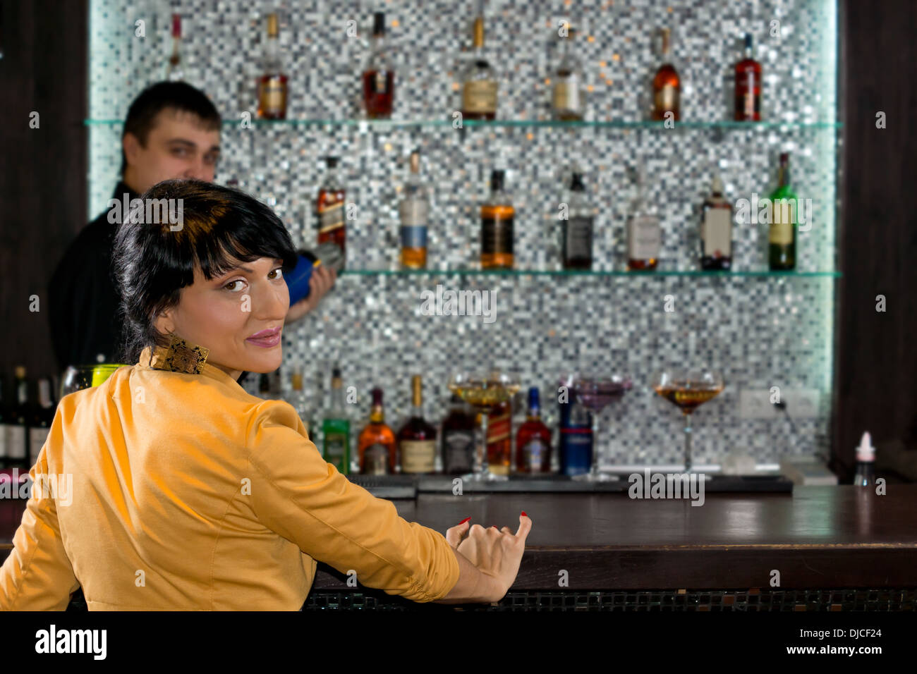 Attractive woman sitting at a bar counter turning to look back over her ...