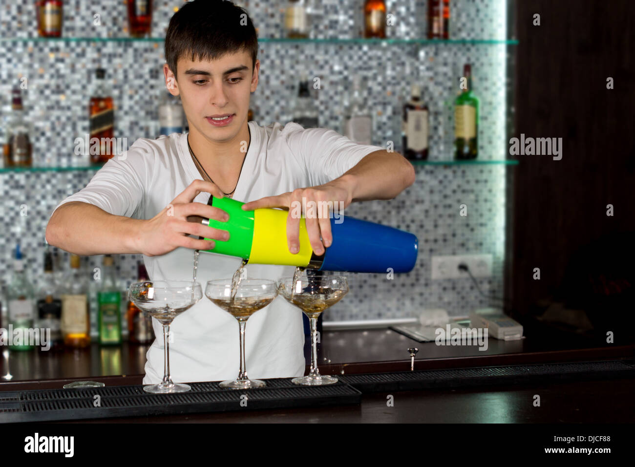 Bartender pouring a cocktail from a colourful cocktail shaker into ...