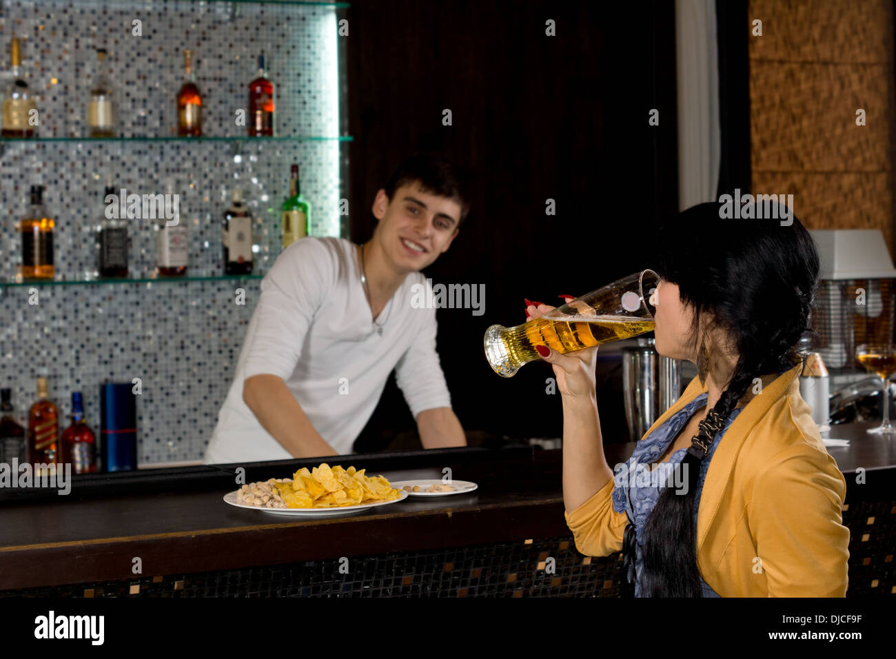 Side view of a young woman drinking a pint of beer in a nightclub with ...