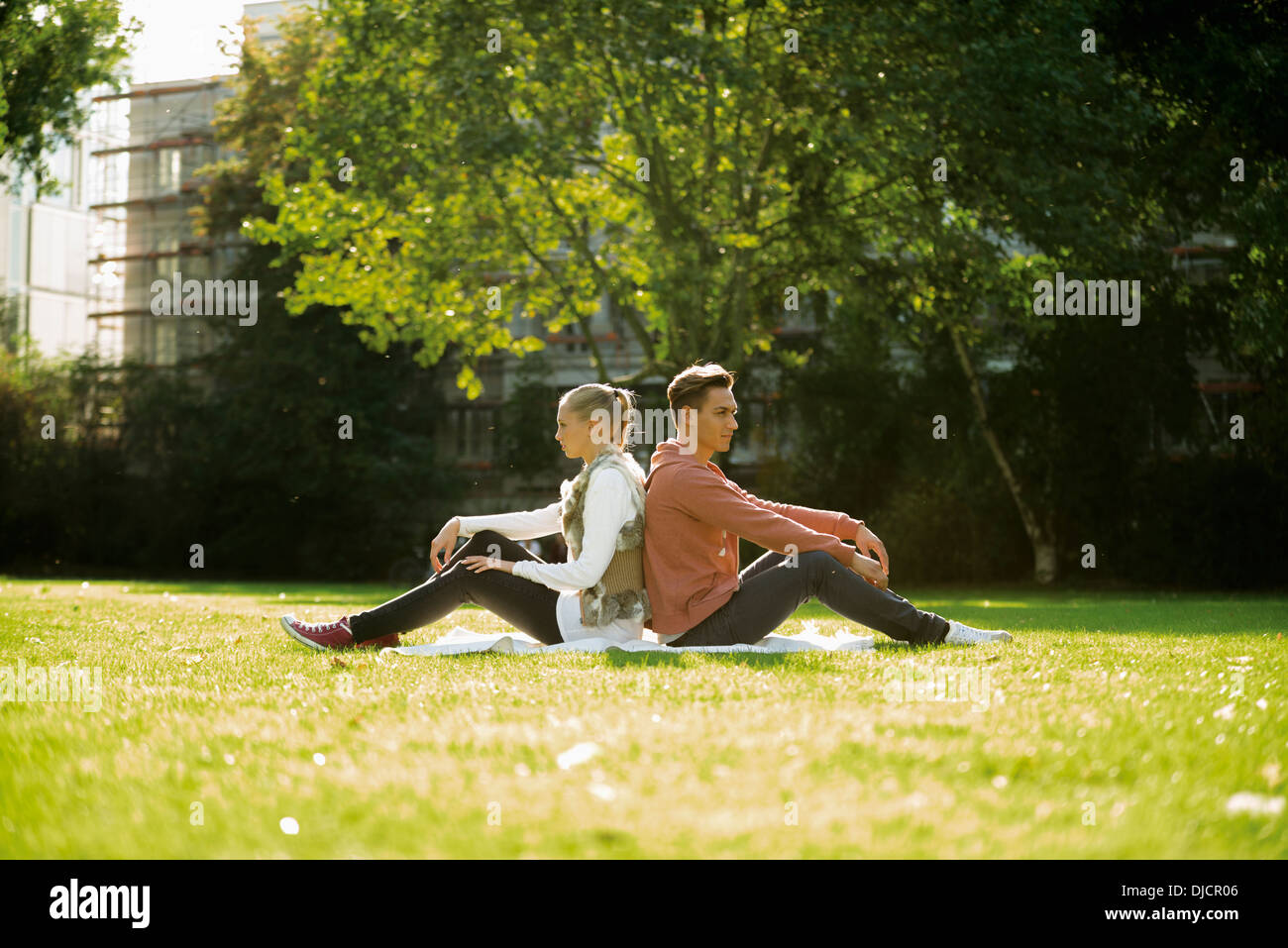 Young couple sitting back to back on a meadow Stock Photo - Alamy