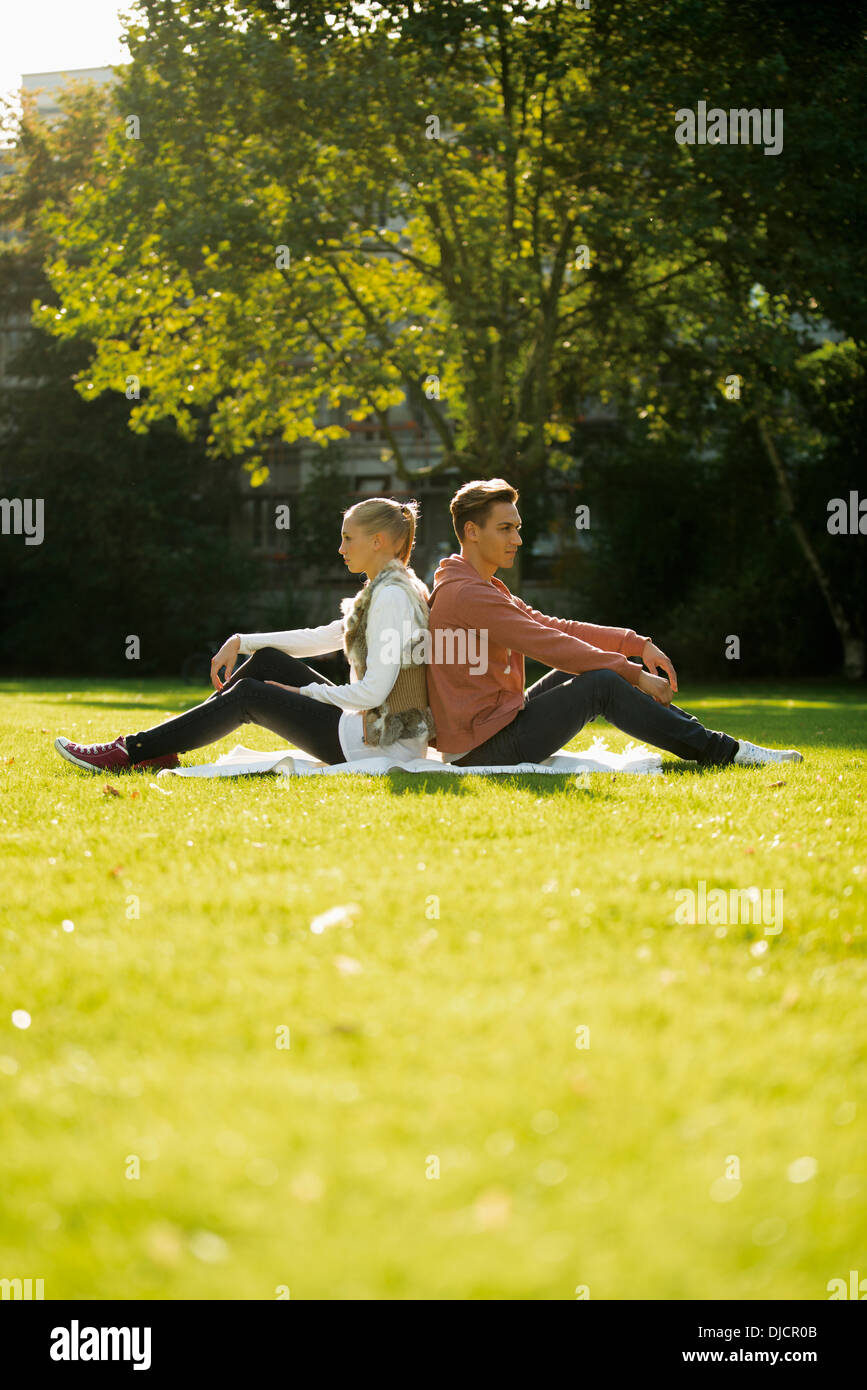 Young couple sitting back to back on a meadow Stock Photo - Alamy