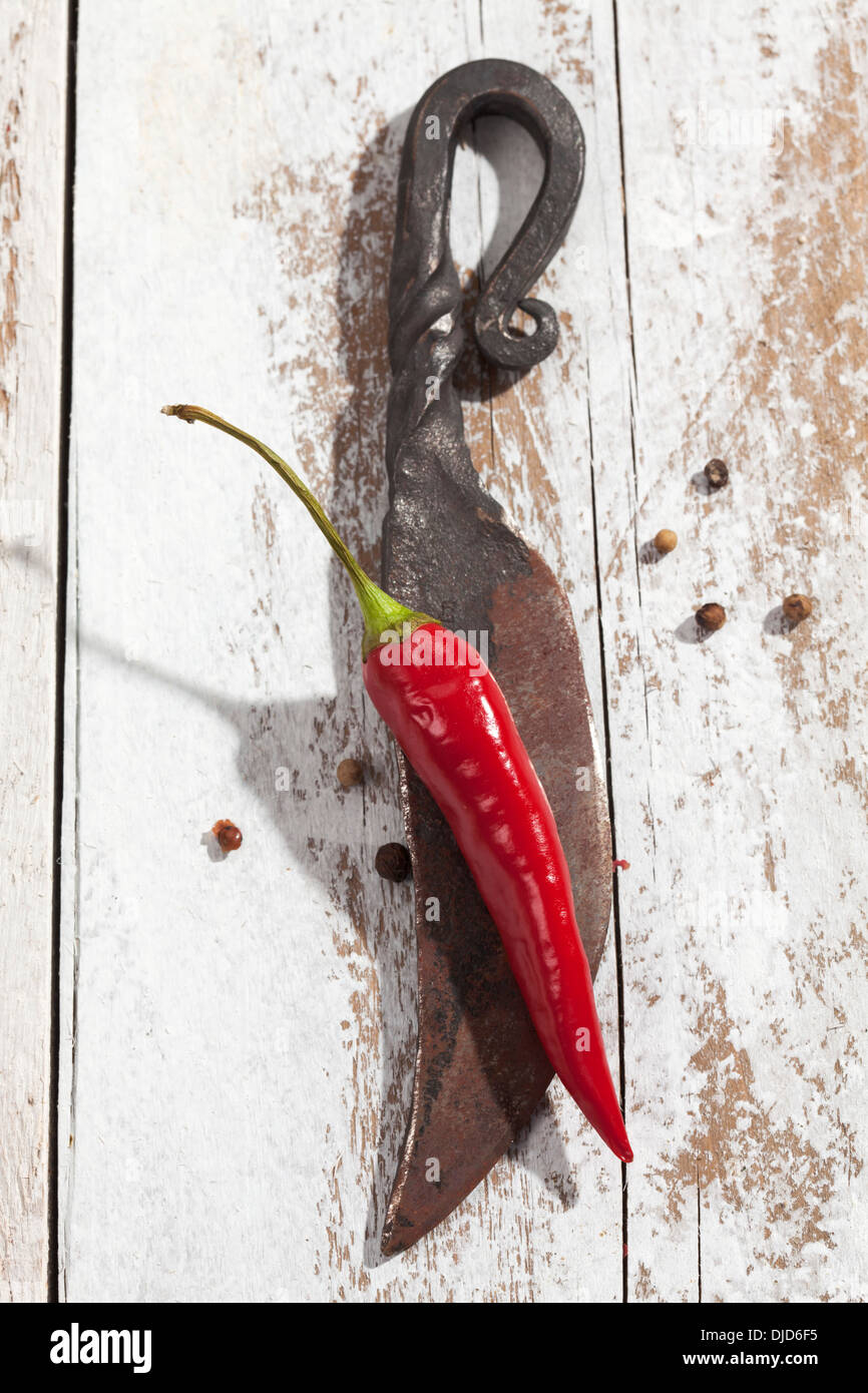 Red chili pepper (Capsicum) and an old knife on white wooden table ...