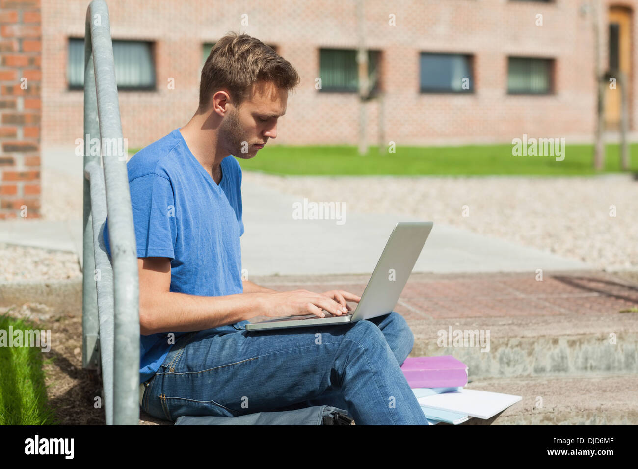 Frowning handsome student sitting on stairs using laptop Stock Photo ...