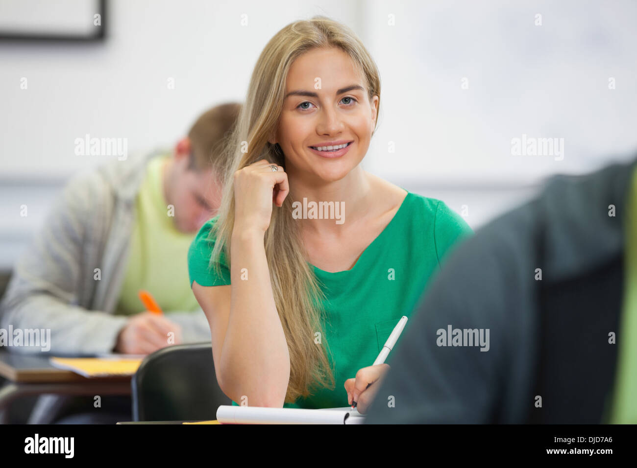 Pretty blonde student taking notes in class smiling at camera Stock ...