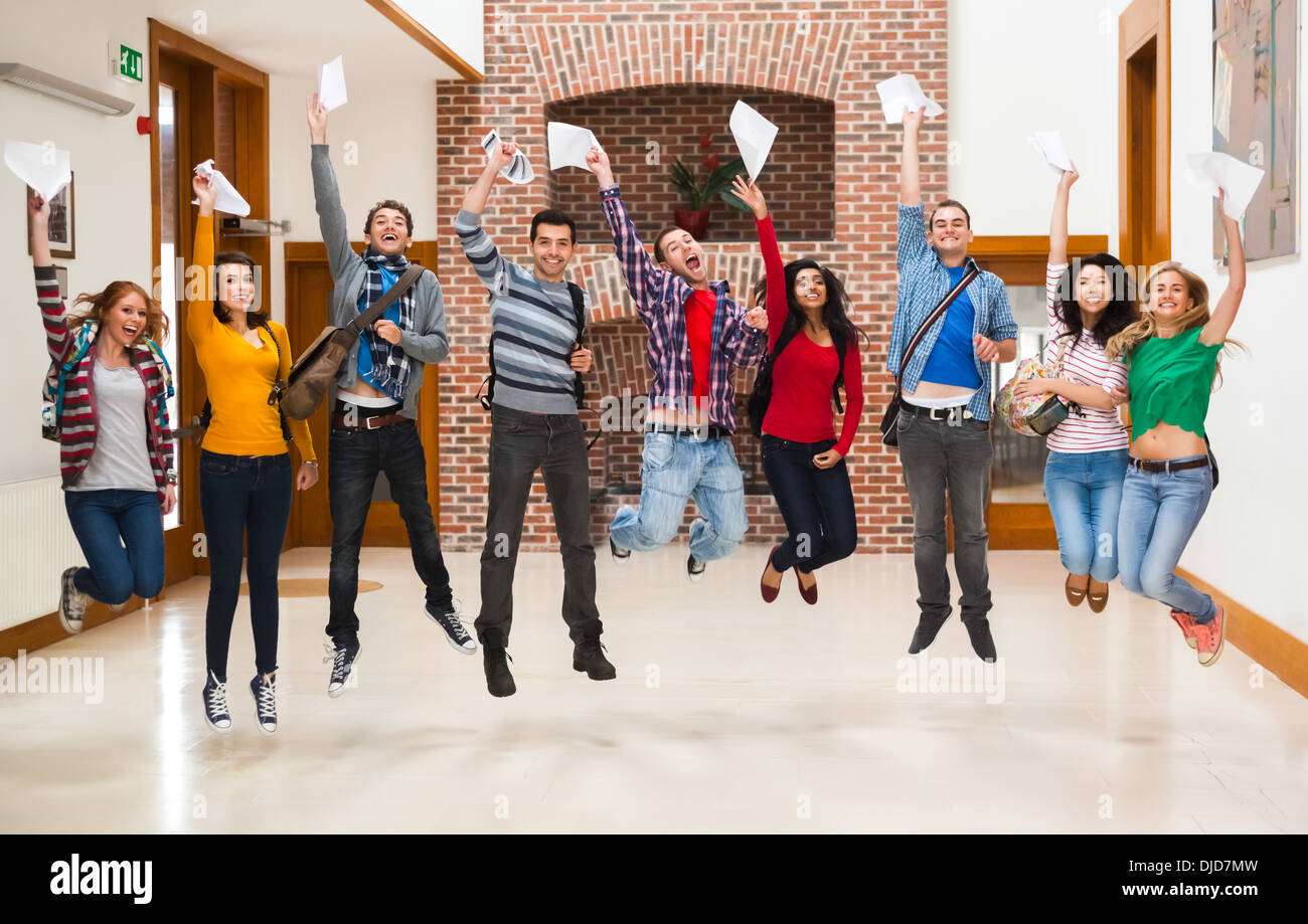 Happy students jumping for joy holding exam results in a hallway Stock ...