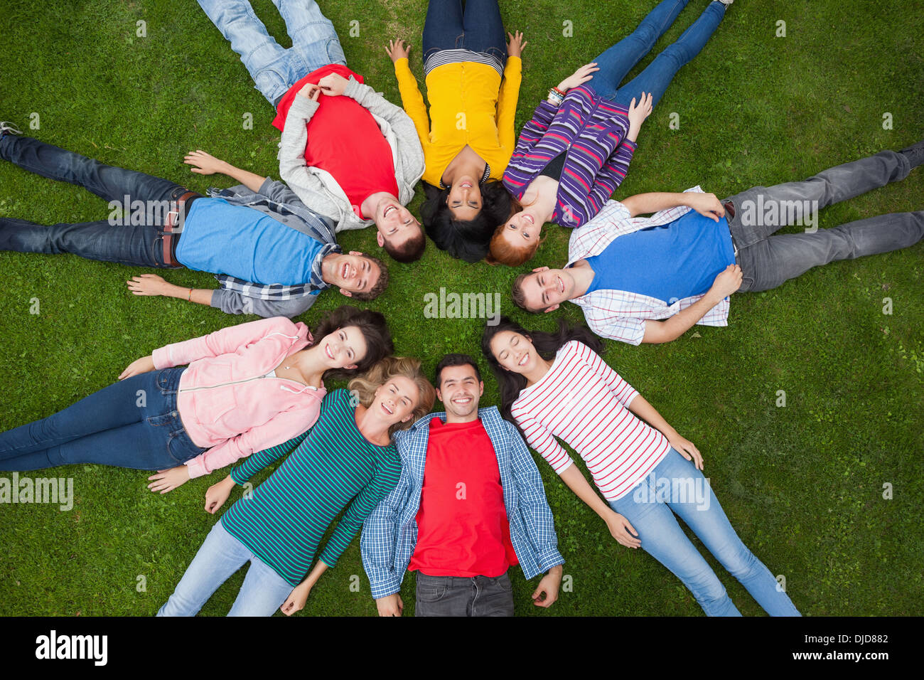Group of students smiling at camera lying in circle on the grass on ...