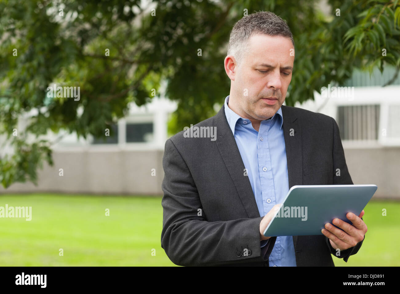 Serious lecturer using his tablet outside on campus Stock Photo - Alamy