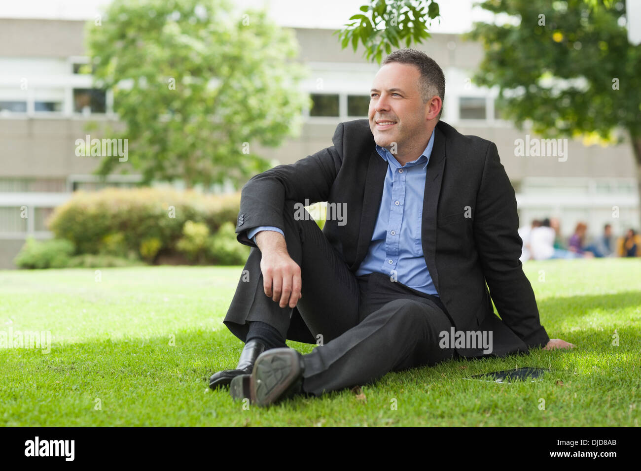 Happy lecturer sitting outside on campus looking away Stock Photo - Alamy
